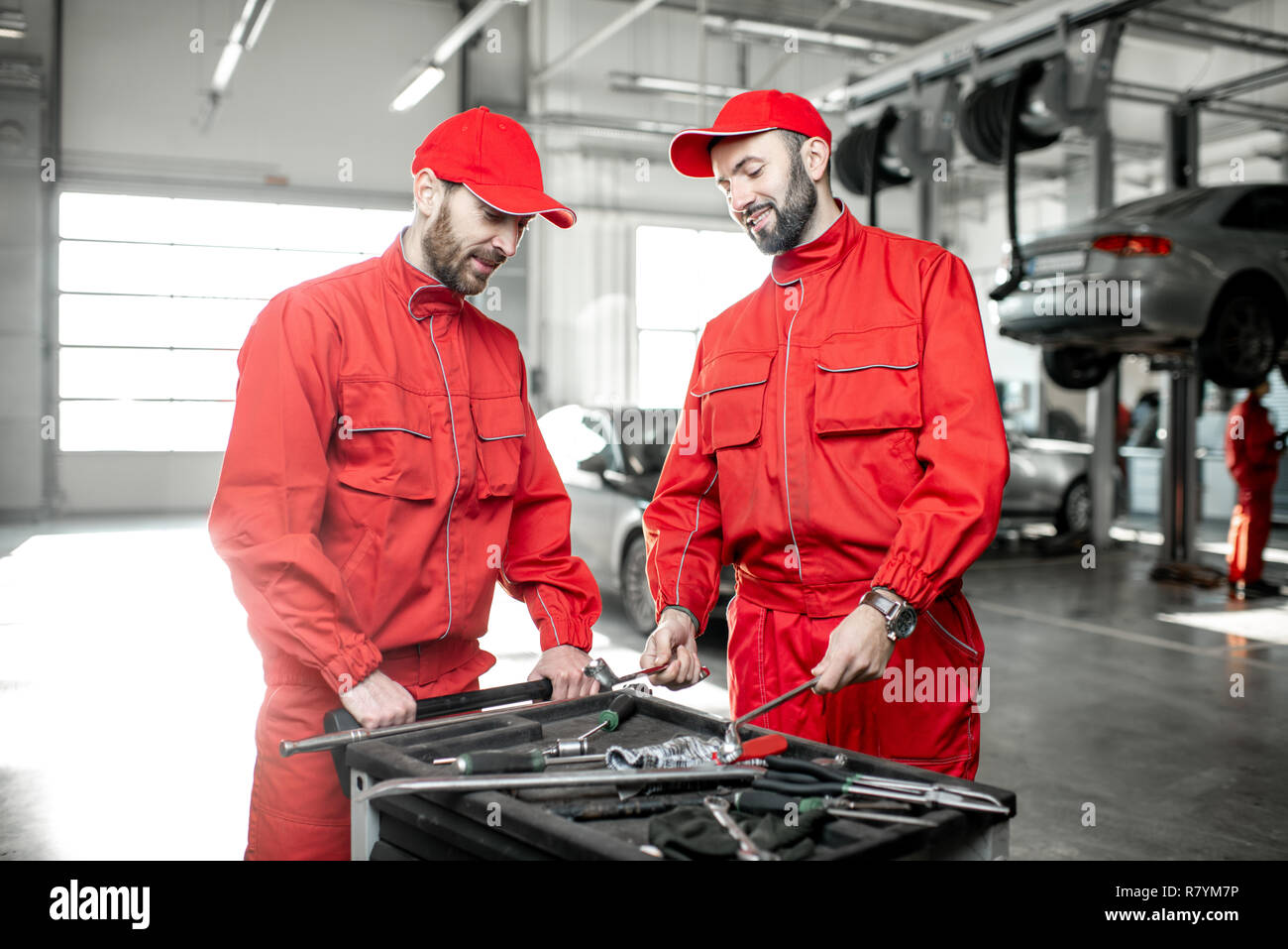 Portrait of a two handsome auto mechanics in red uniform standing with ...
