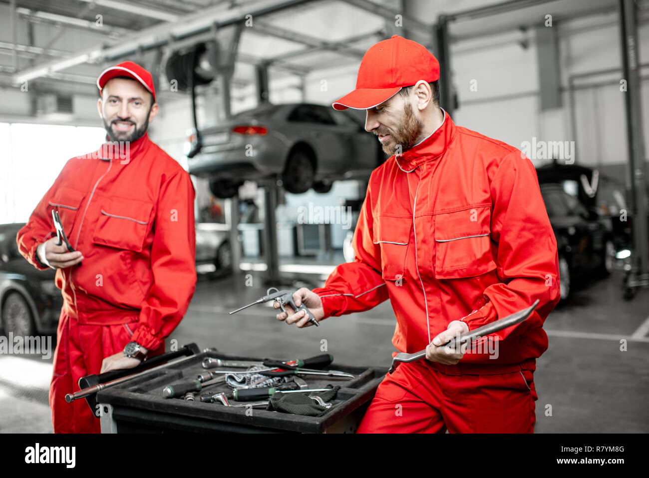 Portrait of a two handsome auto mechanics in red uniform standing with ...