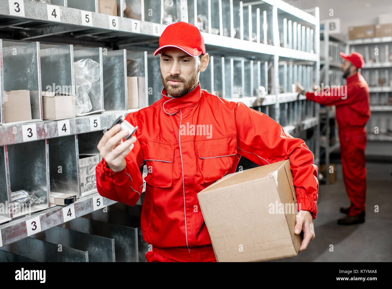 Handsome warehouse worker in red uniform taking some products from the ...