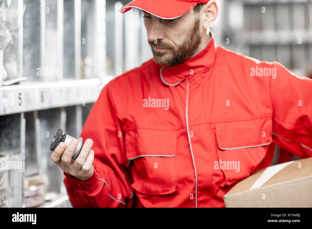 Handsome warehouse worker in red uniform taking some products from the ...