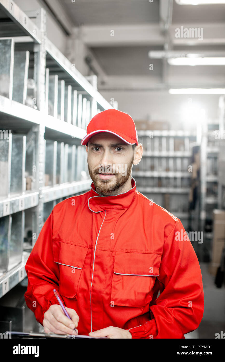 Portrait of a warehouse worker in red uniform filling some documents ...