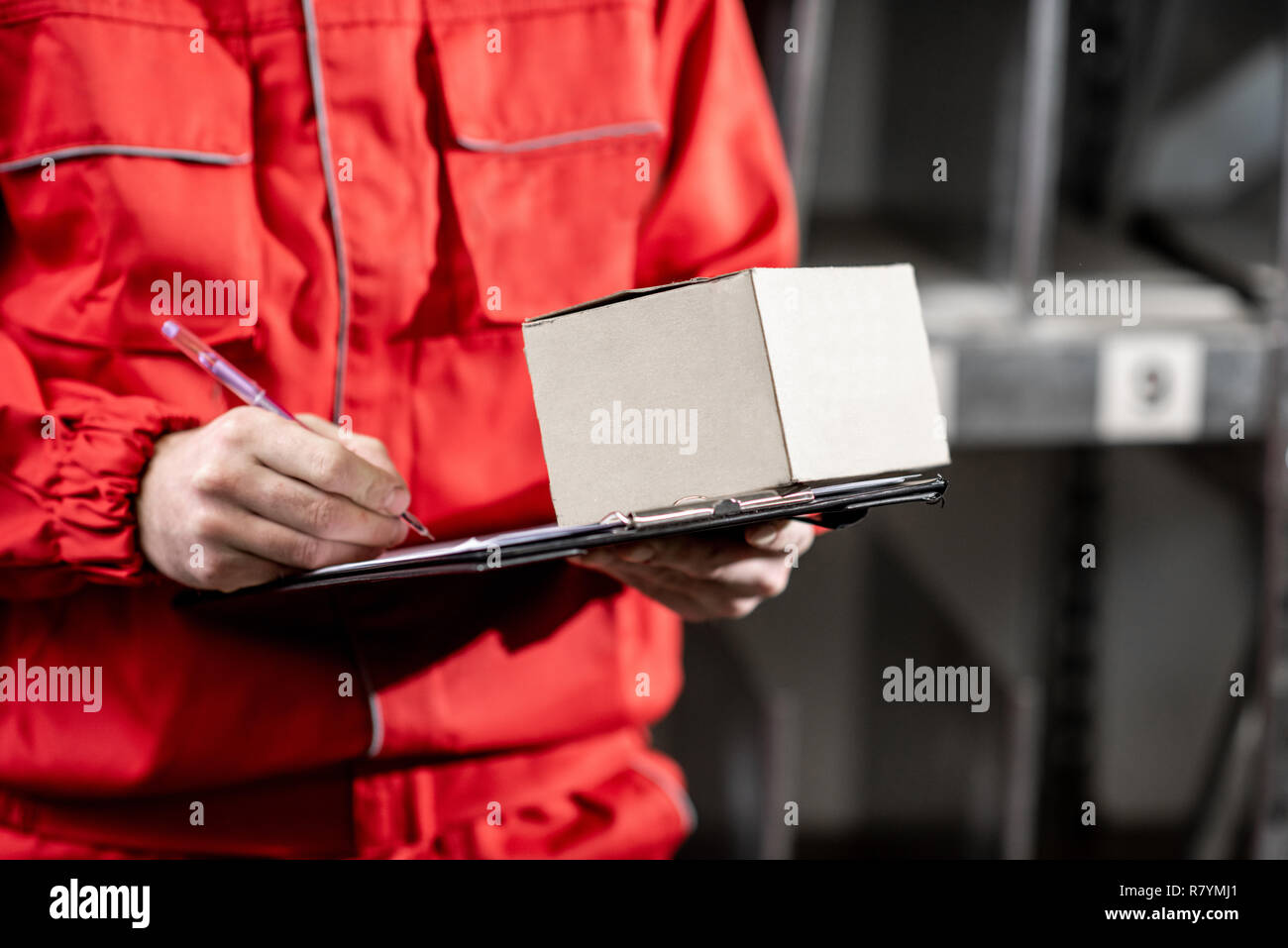 Warehouse worker in red uniform filling some documents checking goods ...