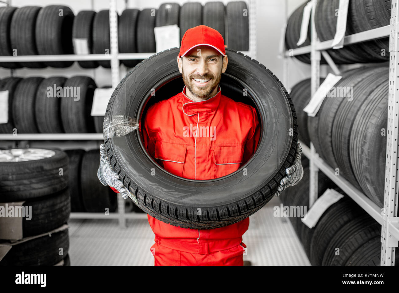 Funny portrait of a smiling worker in red uniform wearing car tire on ...