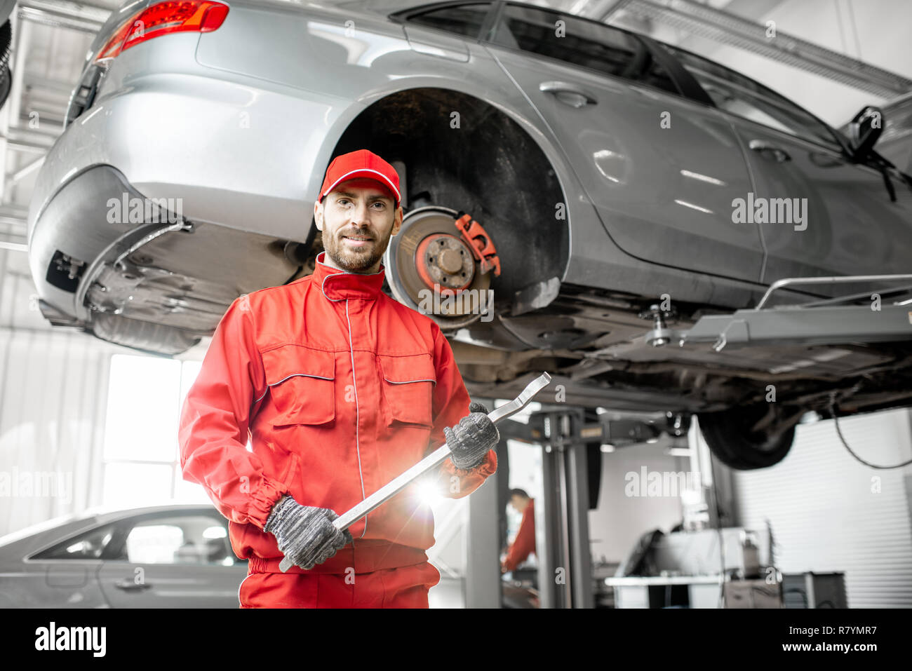Portrait of a handsome auto mechanic in red uniform standing with mount ...