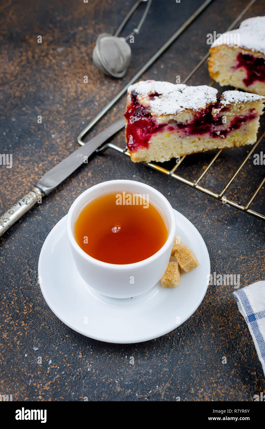 Cherry or plum pie sprinkled with icing sugar, cup of tea on dark ...