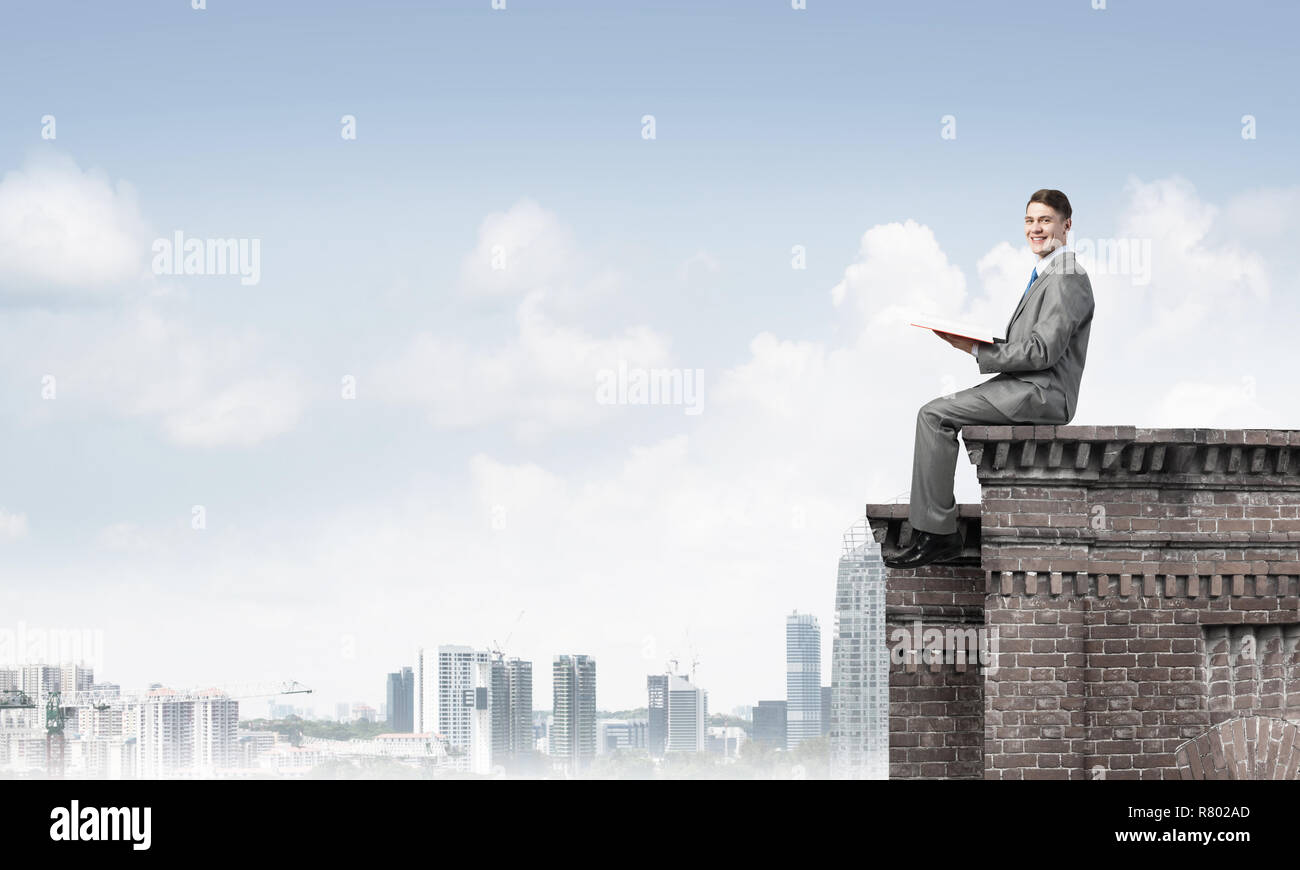 Man on roof edge reading book and cityscape at background Stock Photo ...