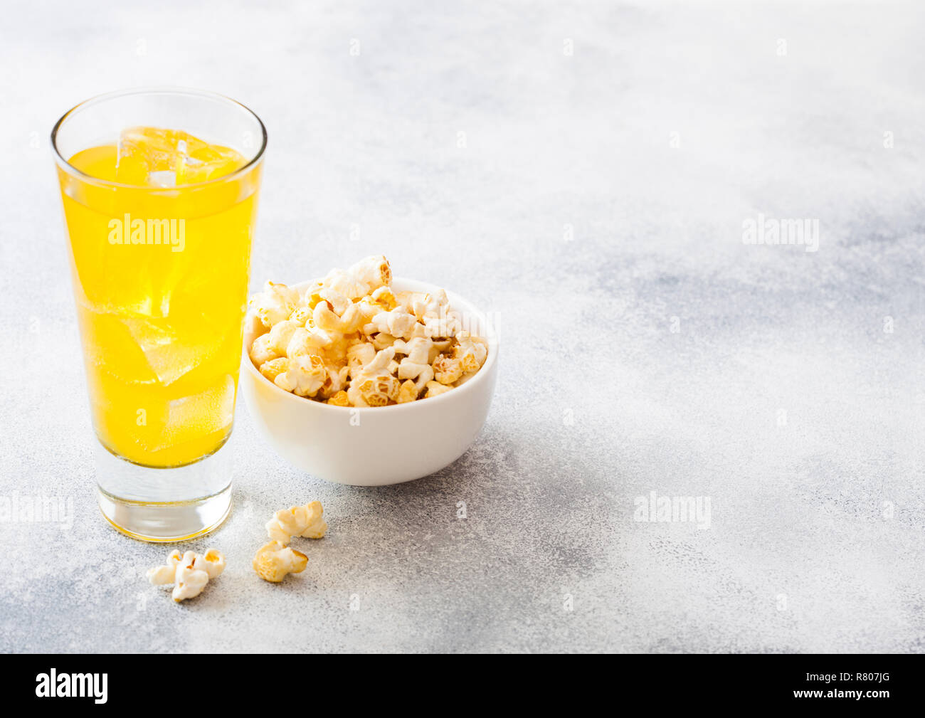 Glass of orange soda drink with ice cubes and whitel bowl of popcorn ...