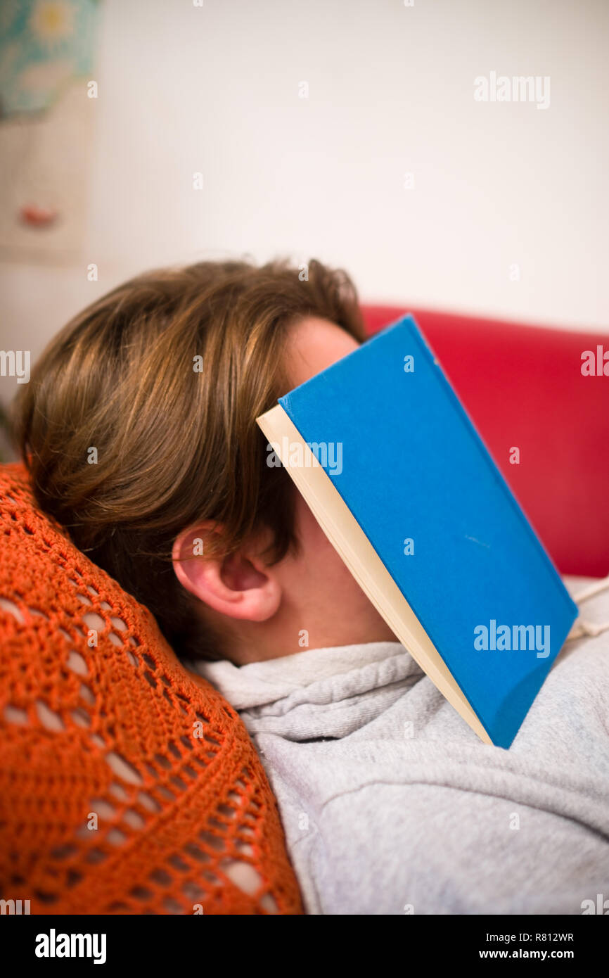 close up side view of a young man lying asleep on a red sofa with a ...