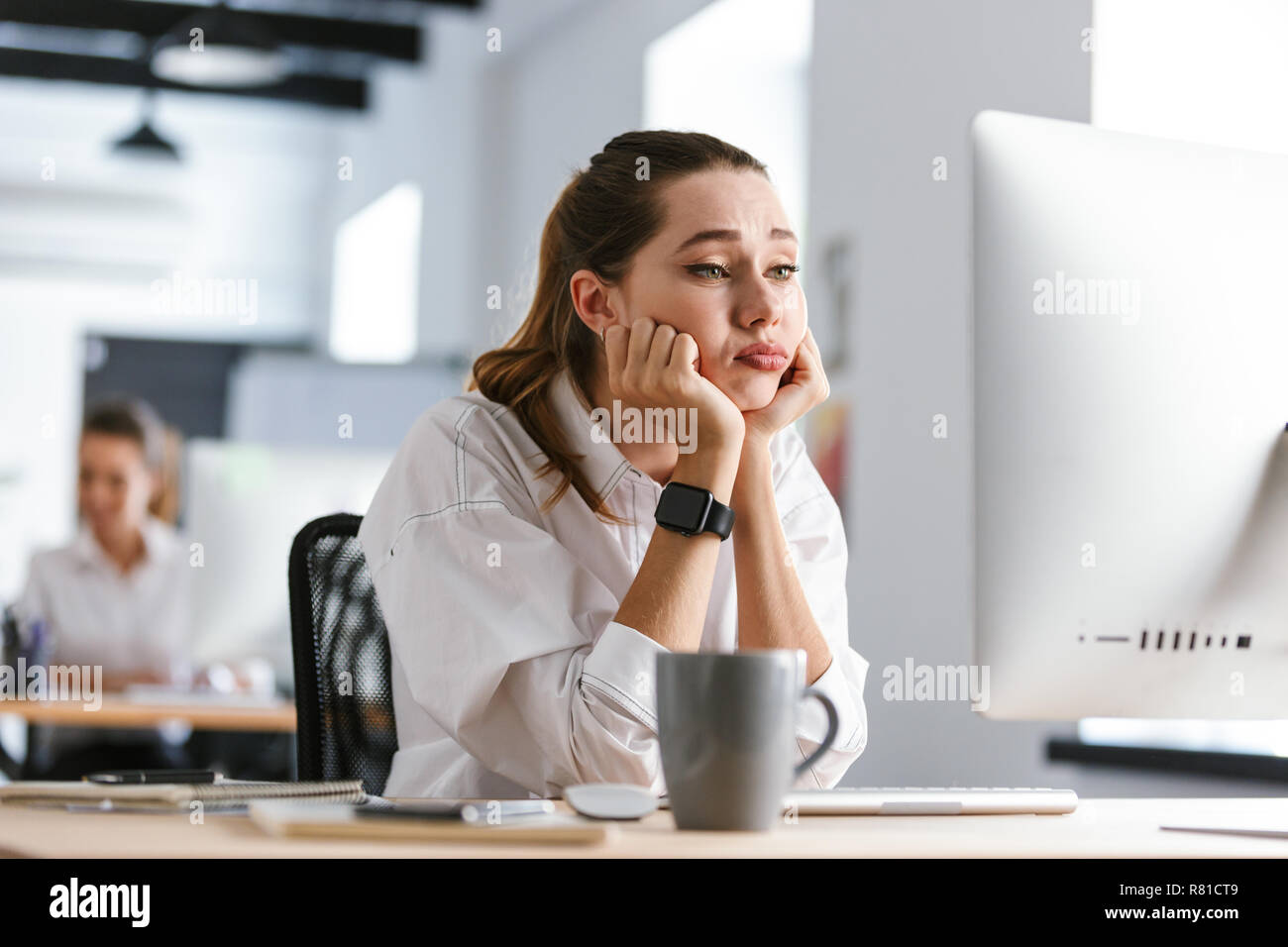 Bored young woman dressed in shirt sitting at her workplace at the ...