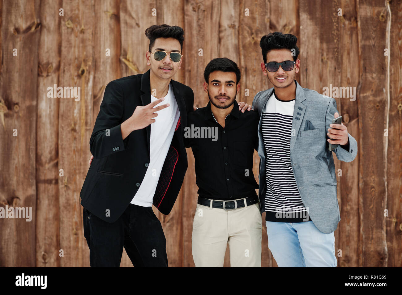 Group of three casual young indian mans posed against wooden background ...