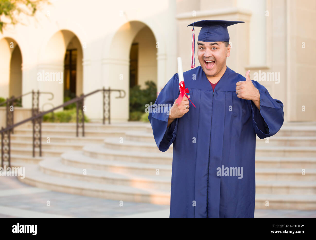 Hispanic Male With Deploma Wearing Graduation Cap and Gown On Campus ...