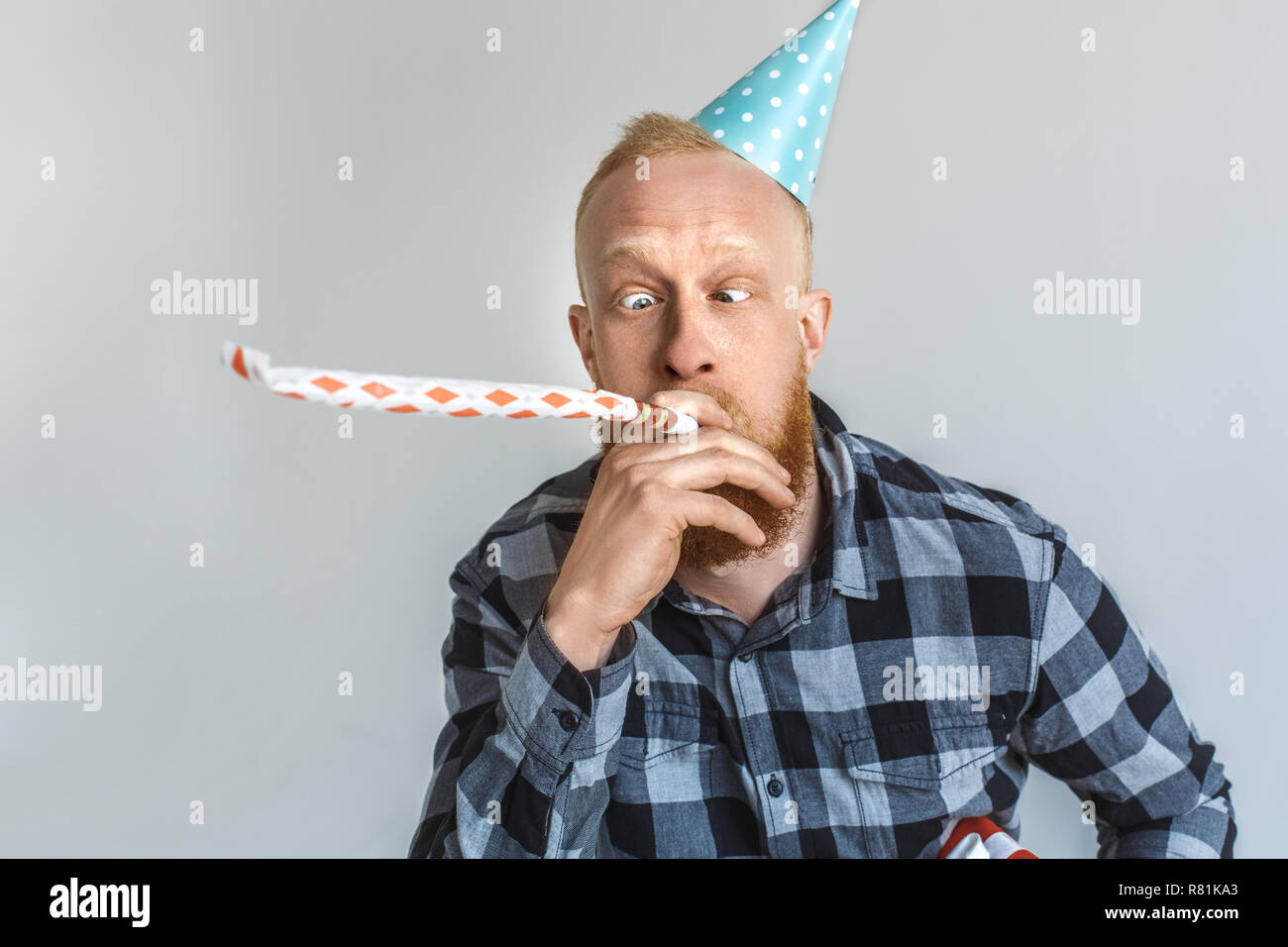 Birthday Concept. Mature man in cap standing isolated on grey blowing ...