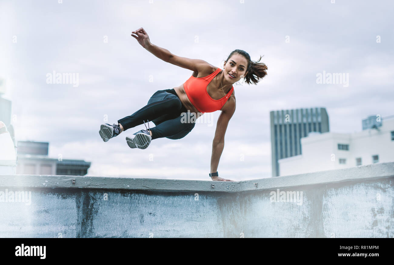 fitness woman jumping on to the terrace from the rooftop fence with one ...