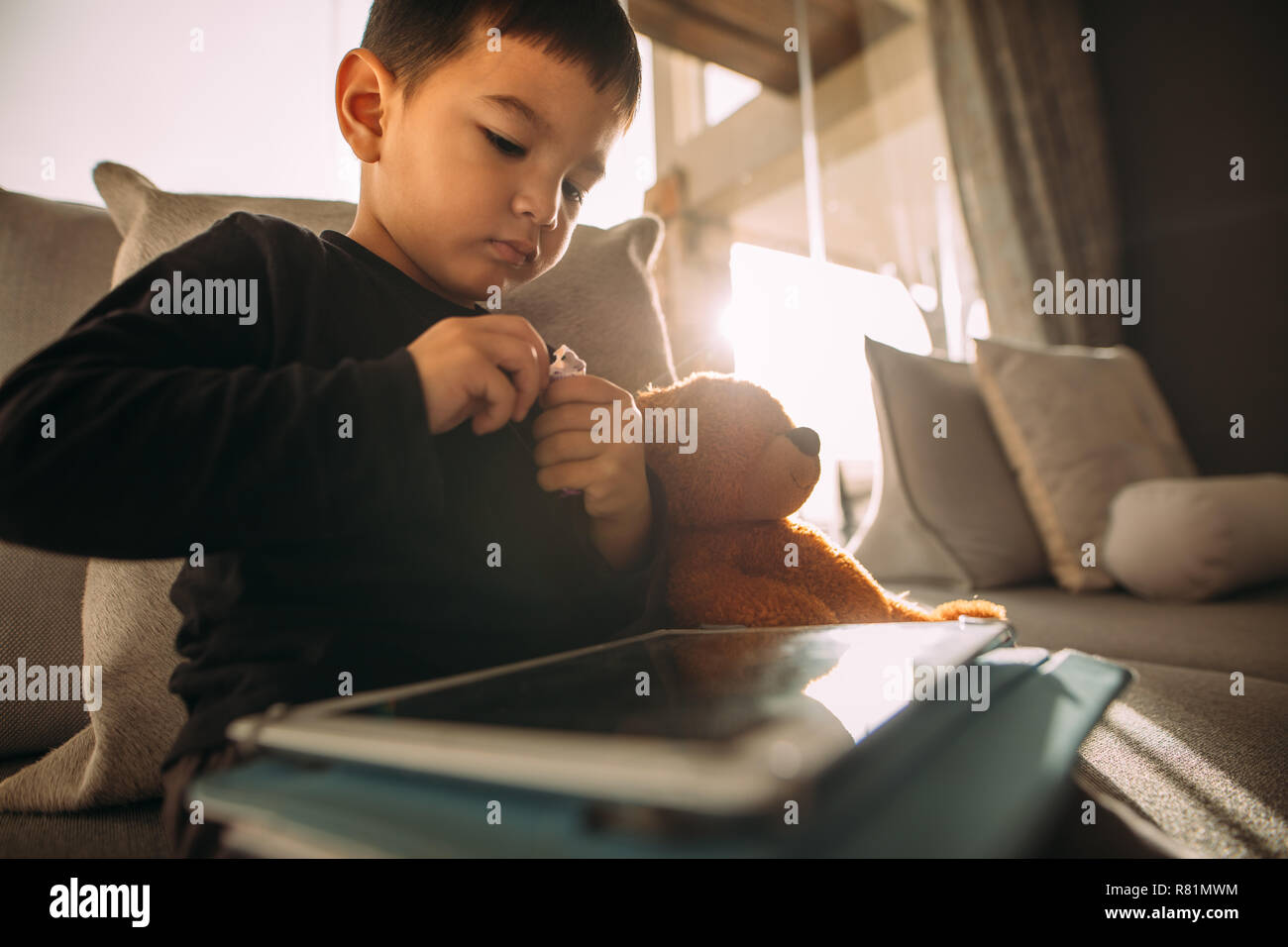 Little boy sitting on sofa with digital tablet eating mint candy ...