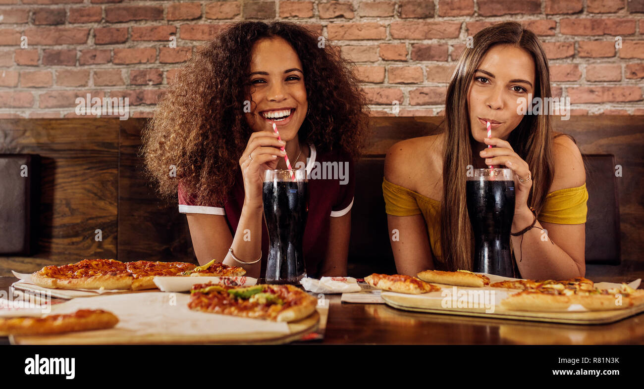 Portrait of two happy young women drinking soft drink at restaurant ...