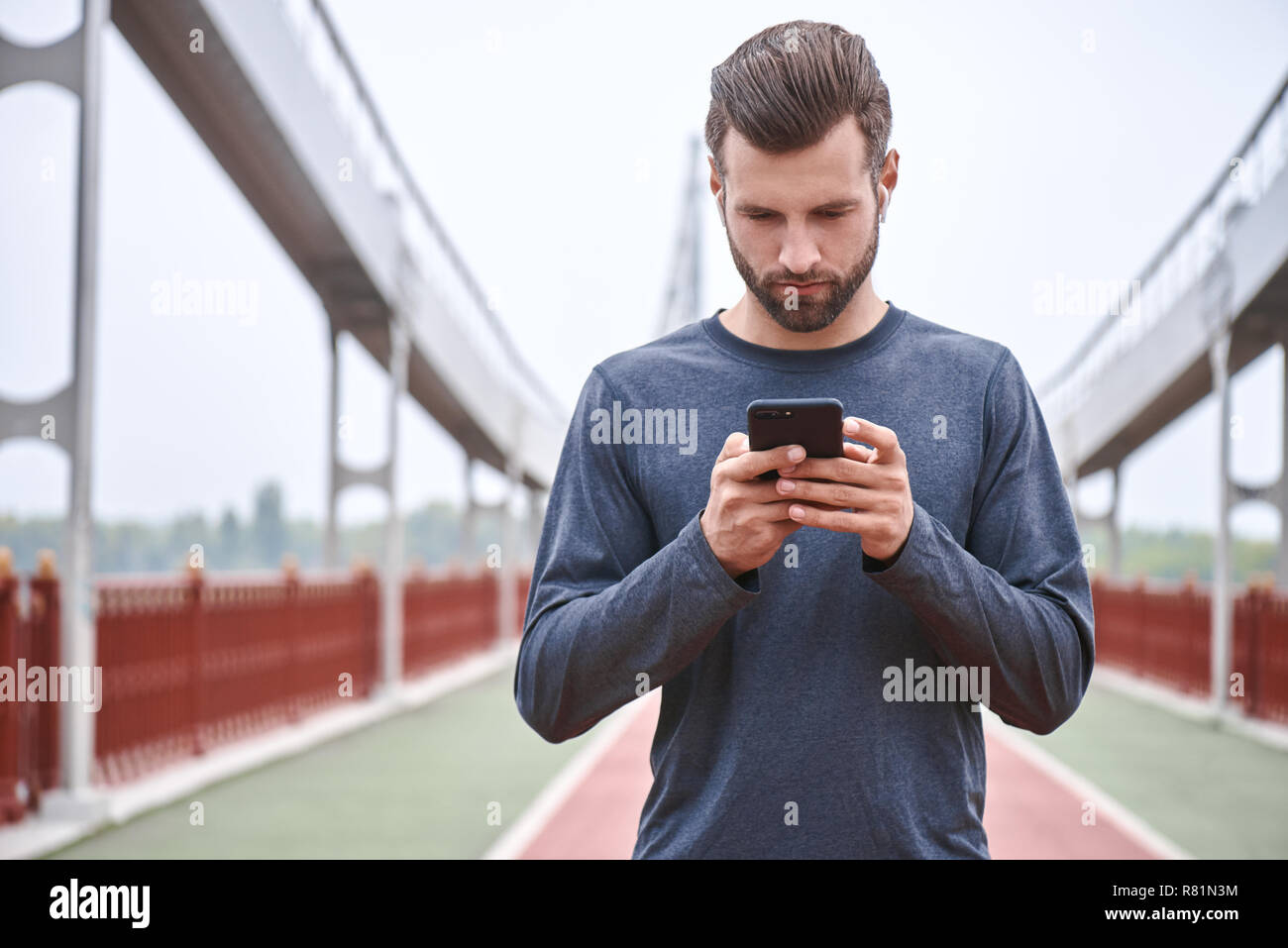 Male runner in white windbreaker typing something on his mobile smart ...