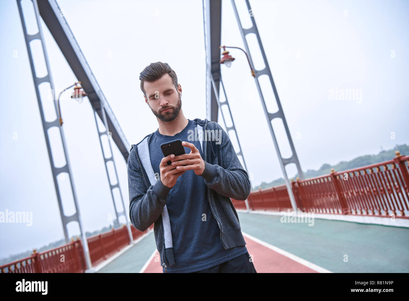 Male runner in white windbreaker typing something on his mobile smart ...