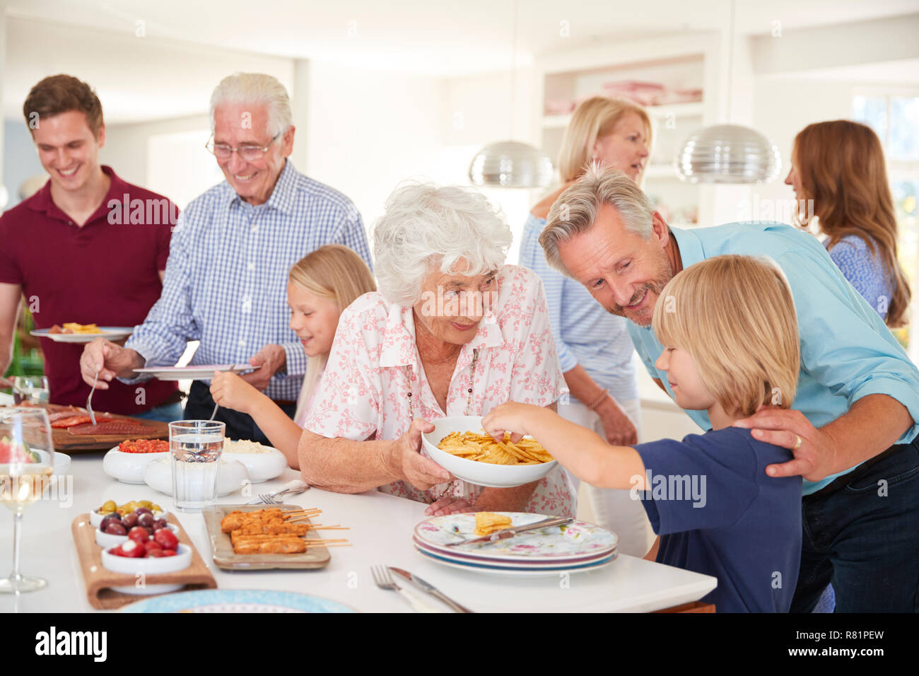 Multi-Generation Family And Friends Eating Food In Kitchen At ...