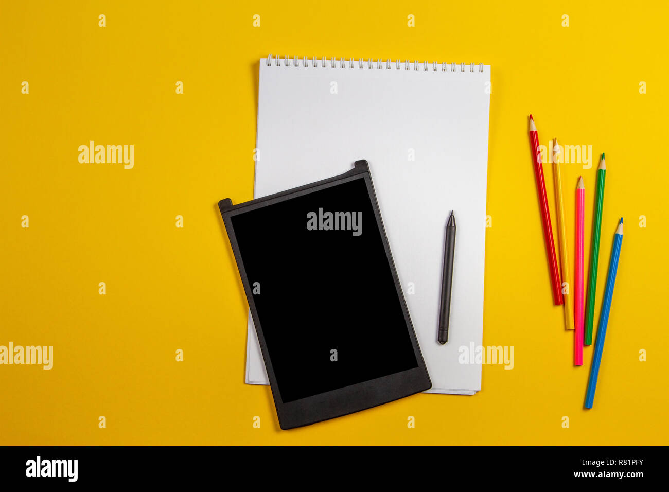 Digital graphic tablet, colored pencils, white paper notebook on yellow ...