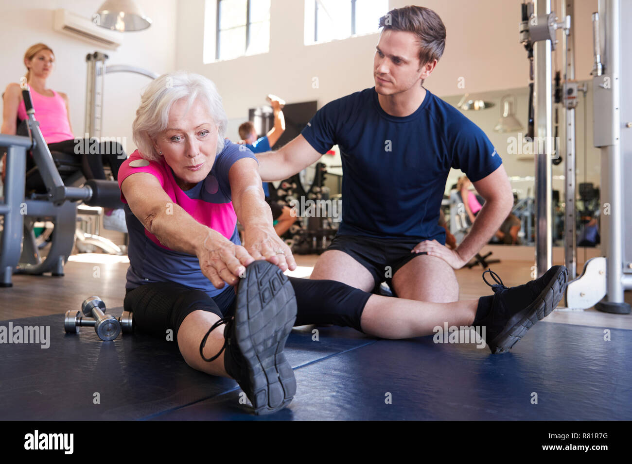 Senior Woman Exercising In Gym Being Encouraged By Personal Trainer ...