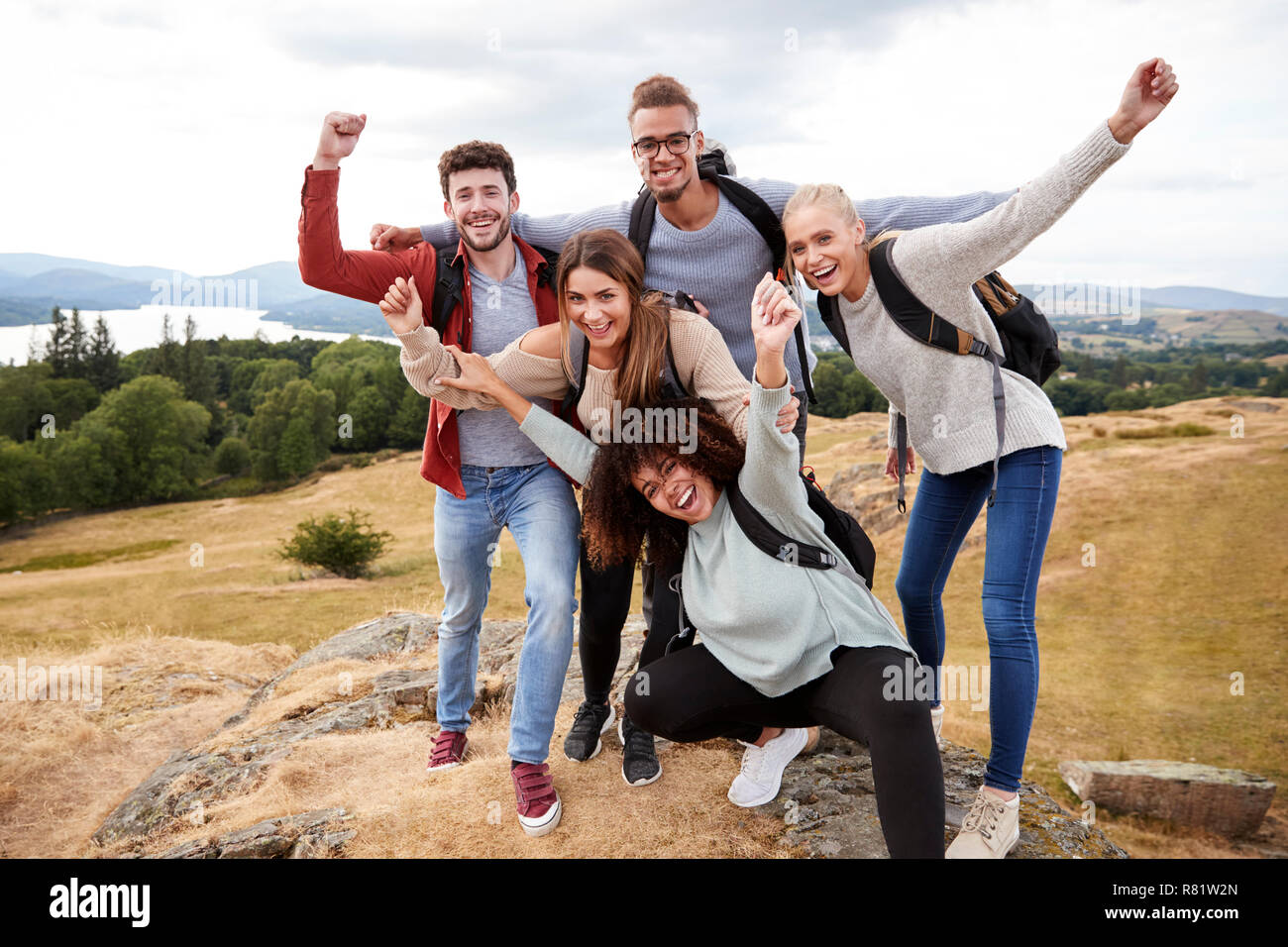 A group of five happy young adult friends cheer at the summit during ...