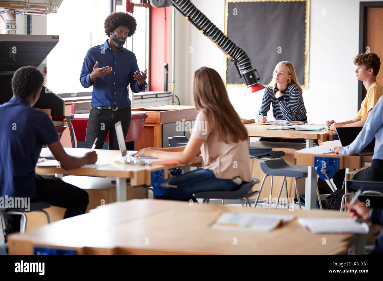 Class Of High School Students Sitting At Work Benches Listening To ...