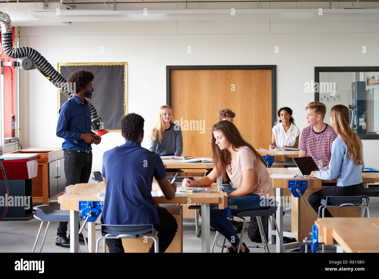 Class Of High School Students Sitting At Work Benches Listening To ...