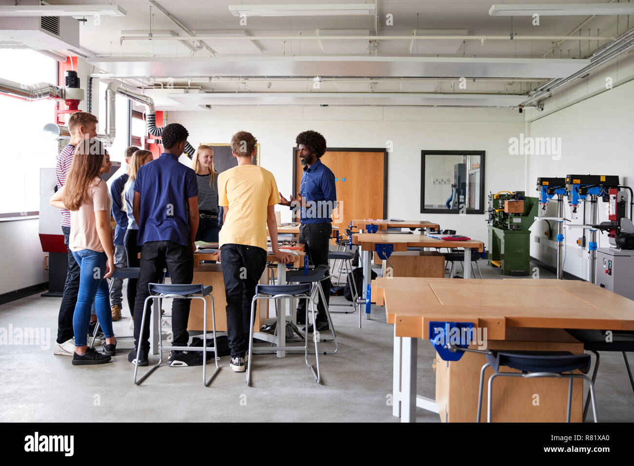 Group Of High School Students Standing Around Work Bench Listening To ...