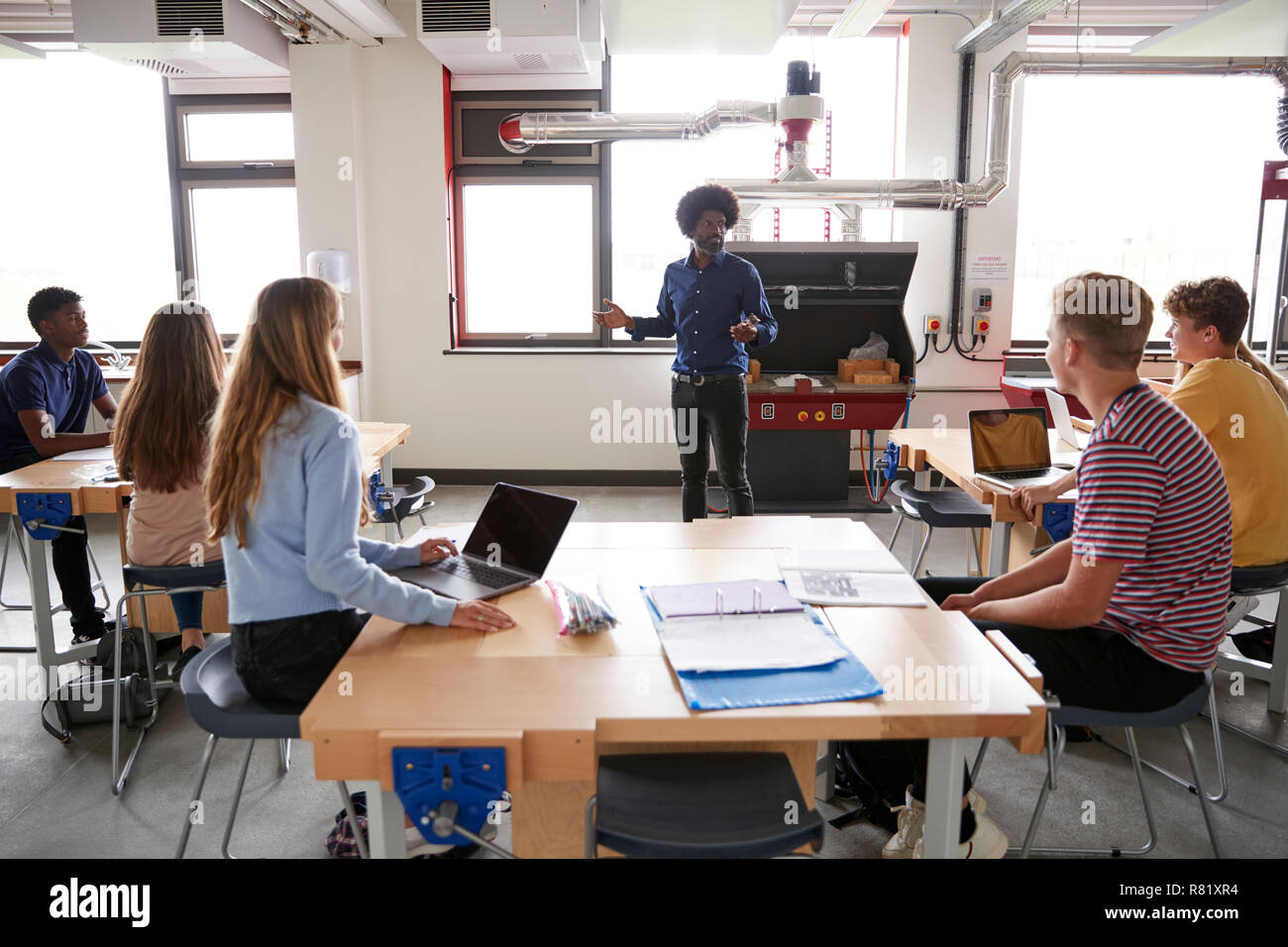 Class Of High School Students Sitting At Work Benches Listening To ...