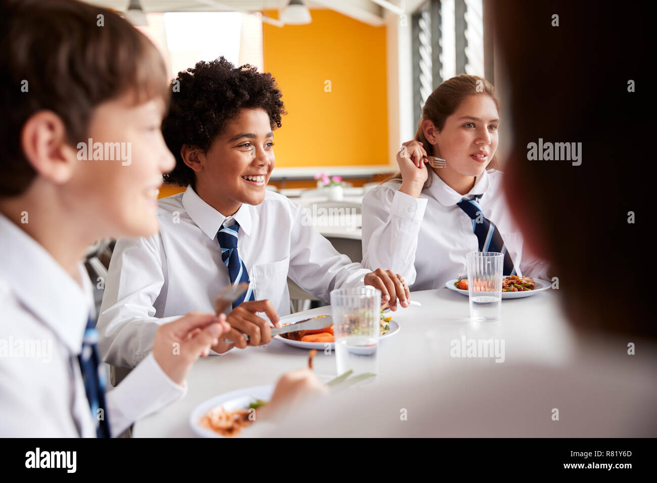 Group Of High School Students Wearing Uniform Sitting Around Table And ...