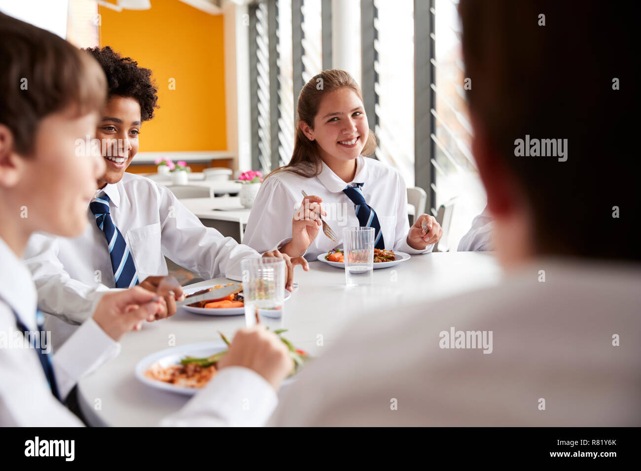 Group Of High School Students Wearing Uniform Sitting Around Table And ...