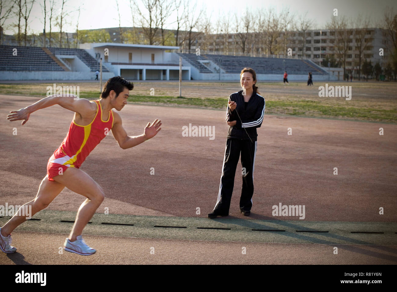 Young adult man running around a track as a mid-adult woman with a stop ...