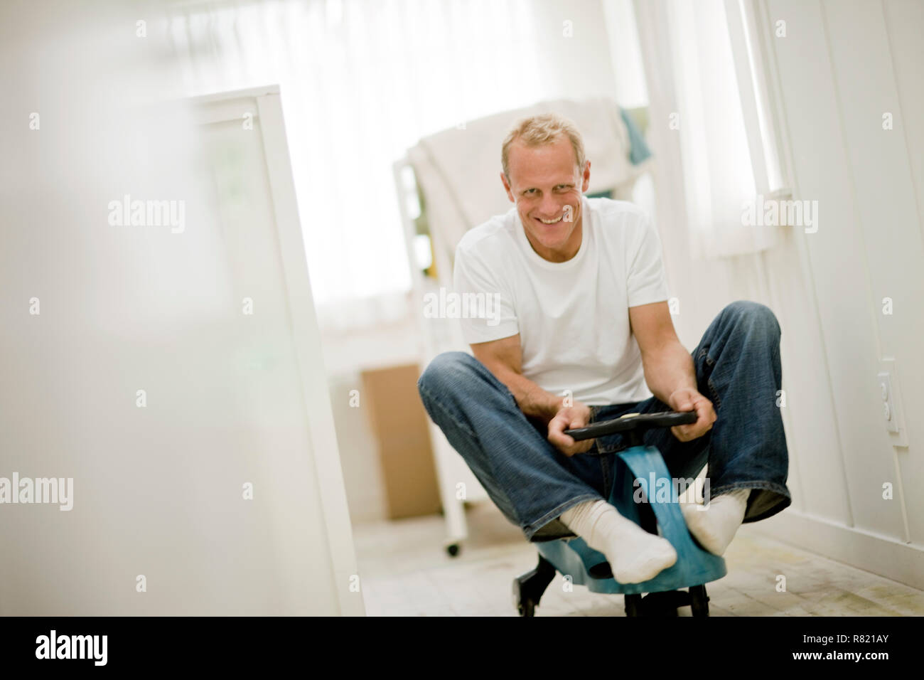 Man riding on toy car in house Stock Photo - Alamy