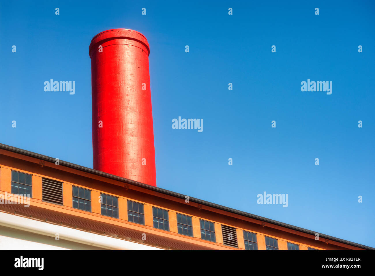Abstract roof line that includes a red smoke stack with a blue sky ...