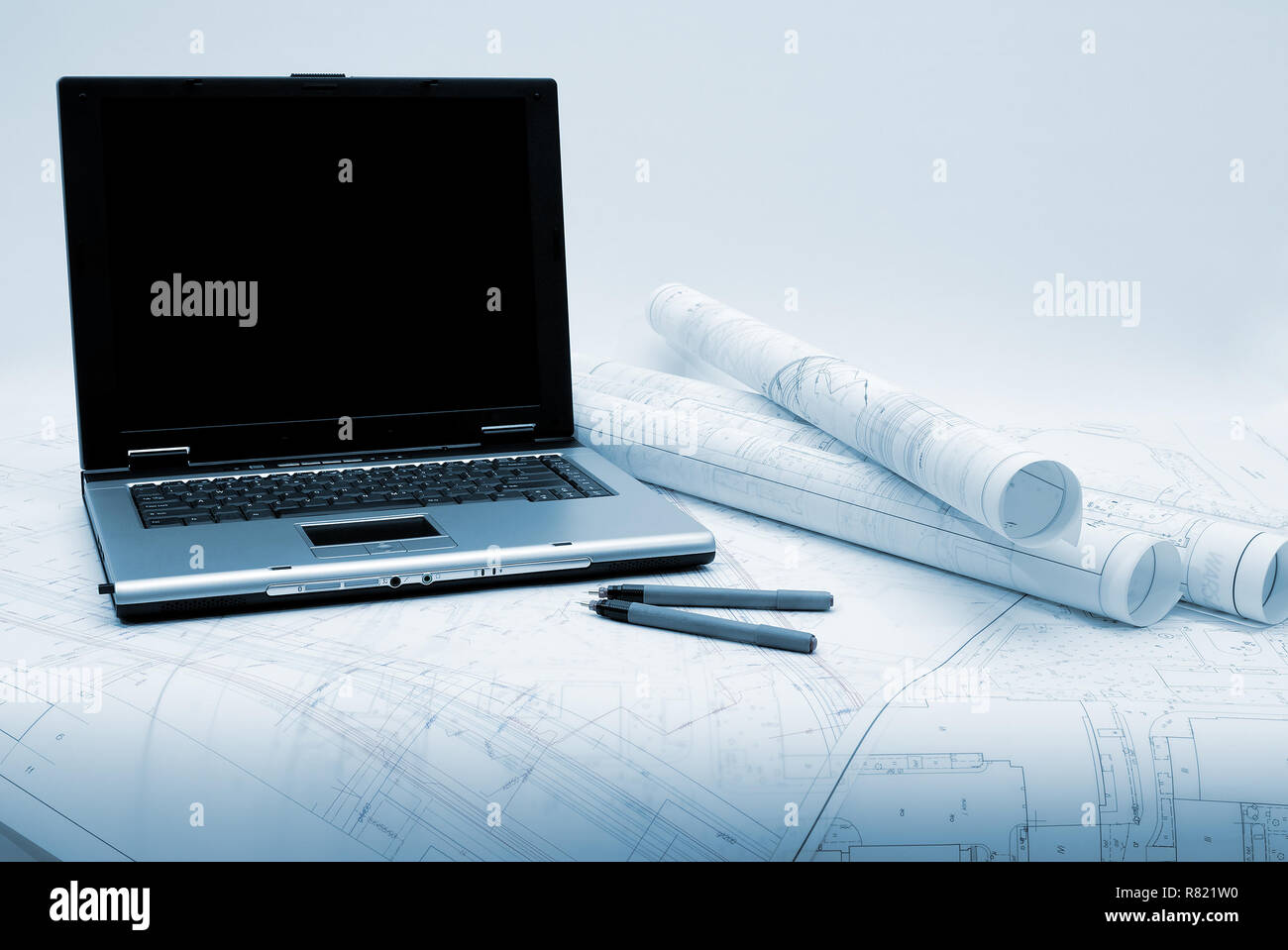 Computer with architectural plans lying on table. Picture in blue tint ...