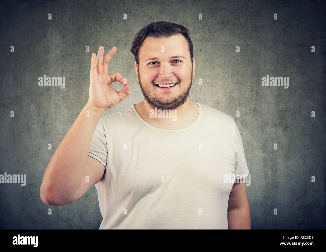Happy chunky man in white t-shirt showing OK sign at camera smiling on ...