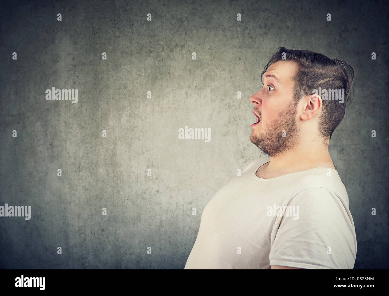 Side view of chubby man in white t-shirt looking away in amazement with ...