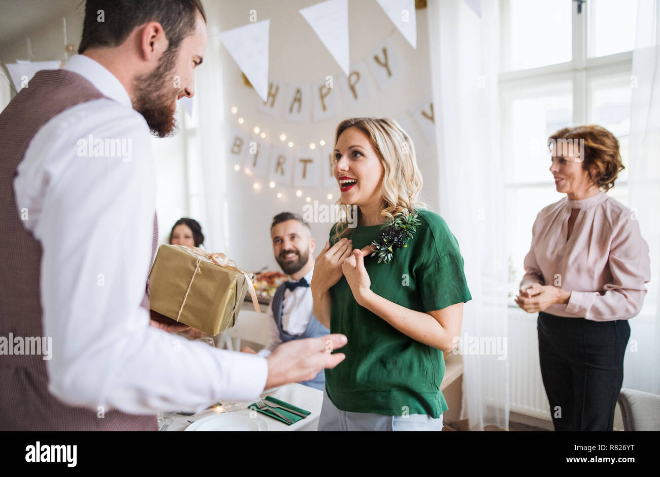 A man giving gift to a young surprised woman on a family birthday party ...