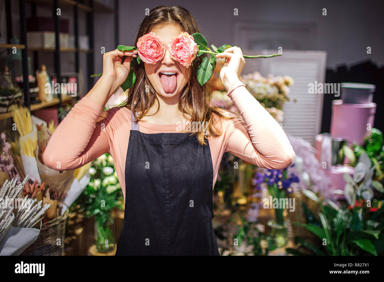 Funny and positive young female florist cover eyes with roses and show ...