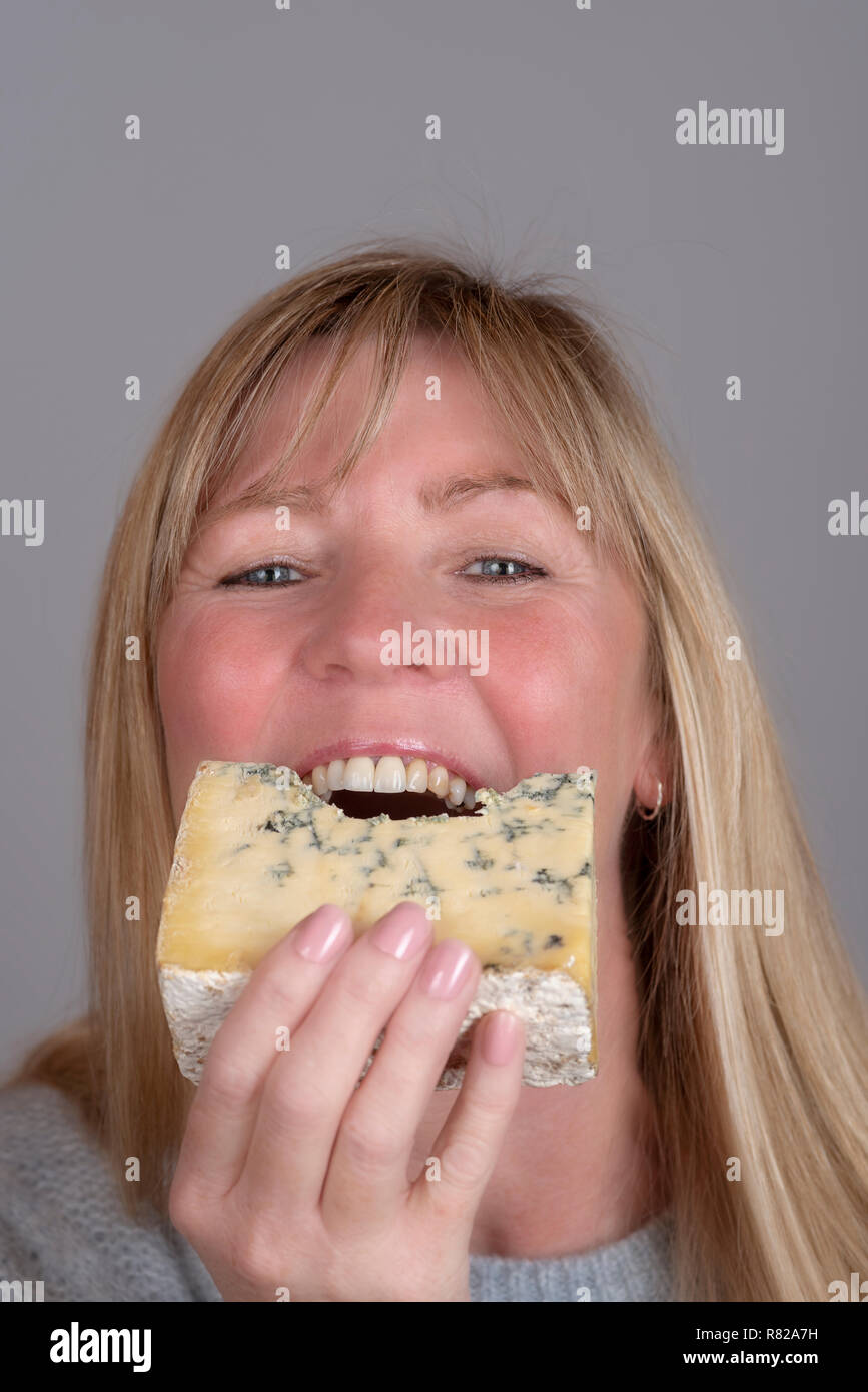 Blonde woman eating and enjoying a wedge of blue cheese Stock Photo - Alamy