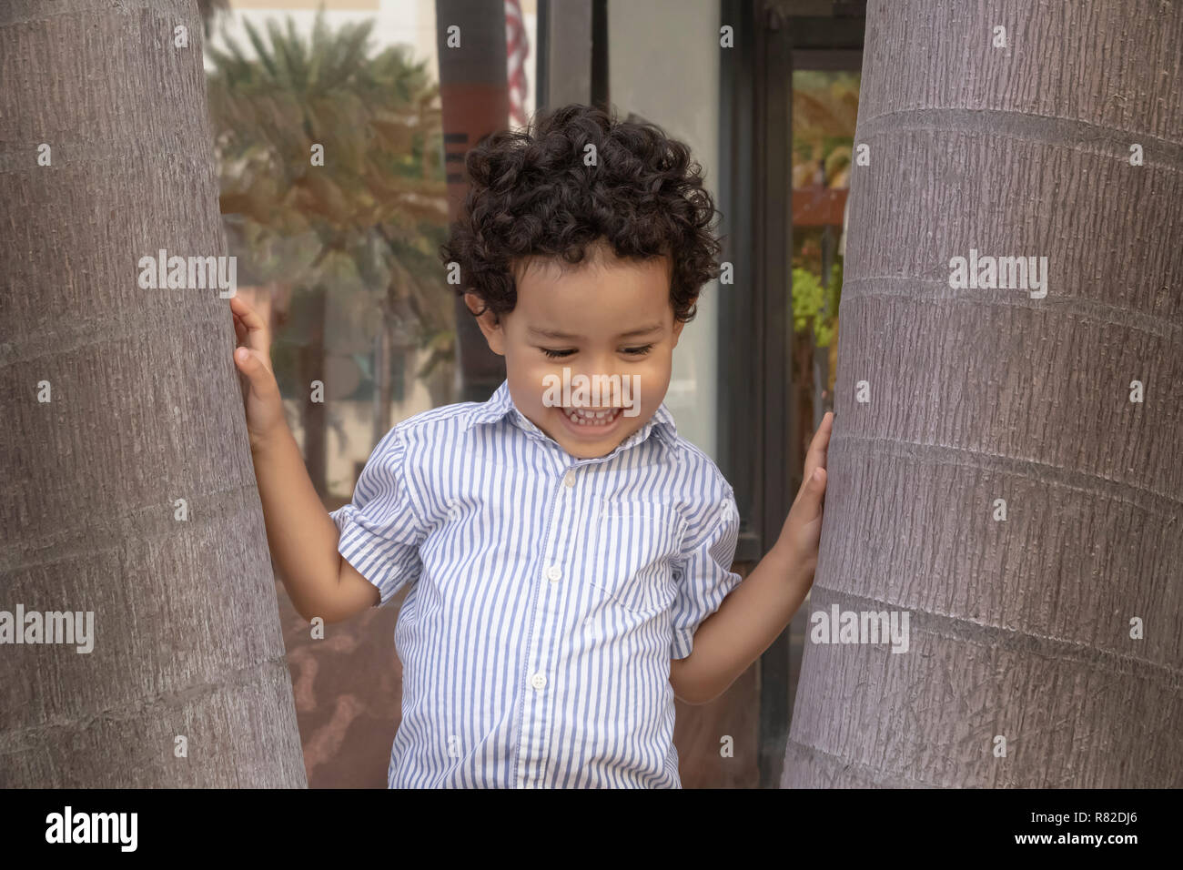 A boy stands between two trees with a happy smile looking down ...