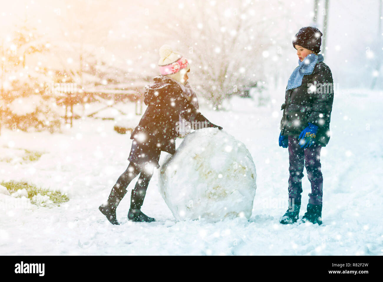 Children boy and girl outdoors in snowy winter are making a big snowman ...