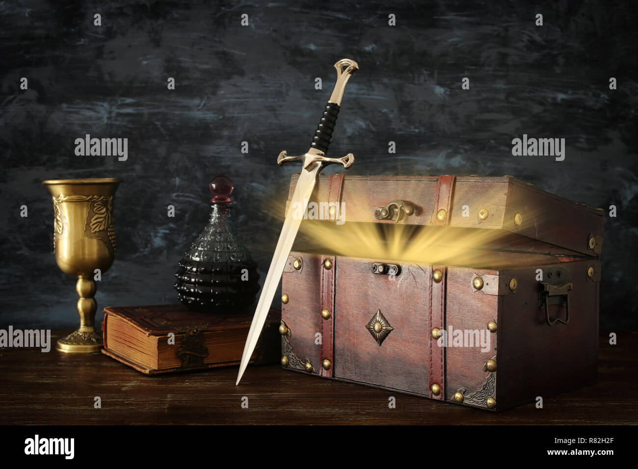 low key image of open chest with treasure, wine cup, antique old book ...