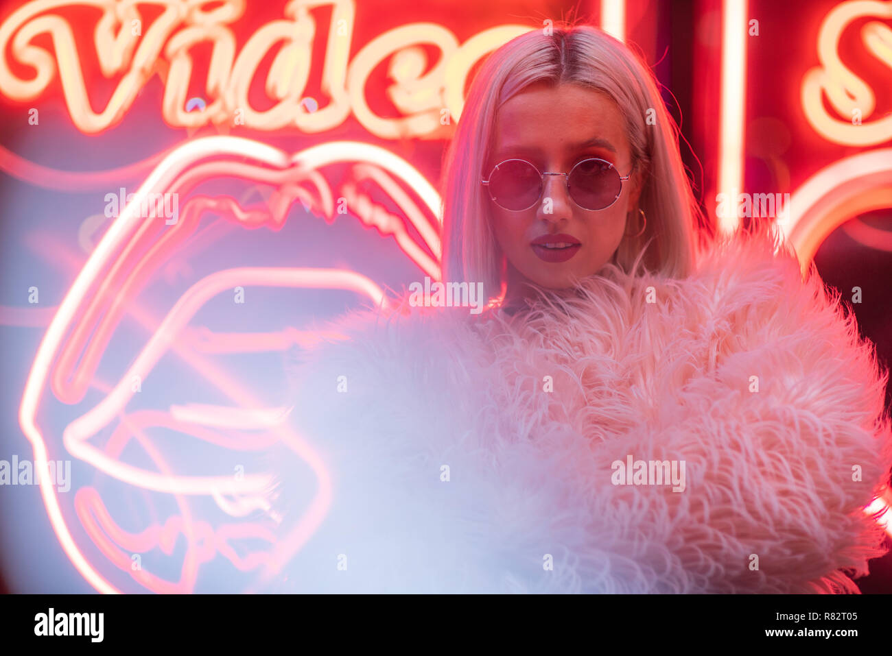 Cinematic portrait of blond girl with furry pink coat on neon sign at ...