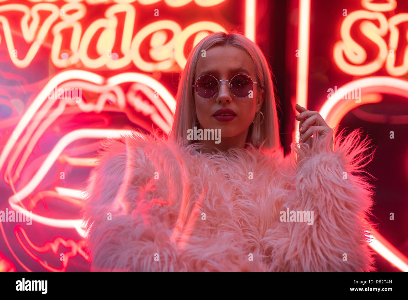 Cinematic portrait of blond girl with furry pink coat on neon sign at ...