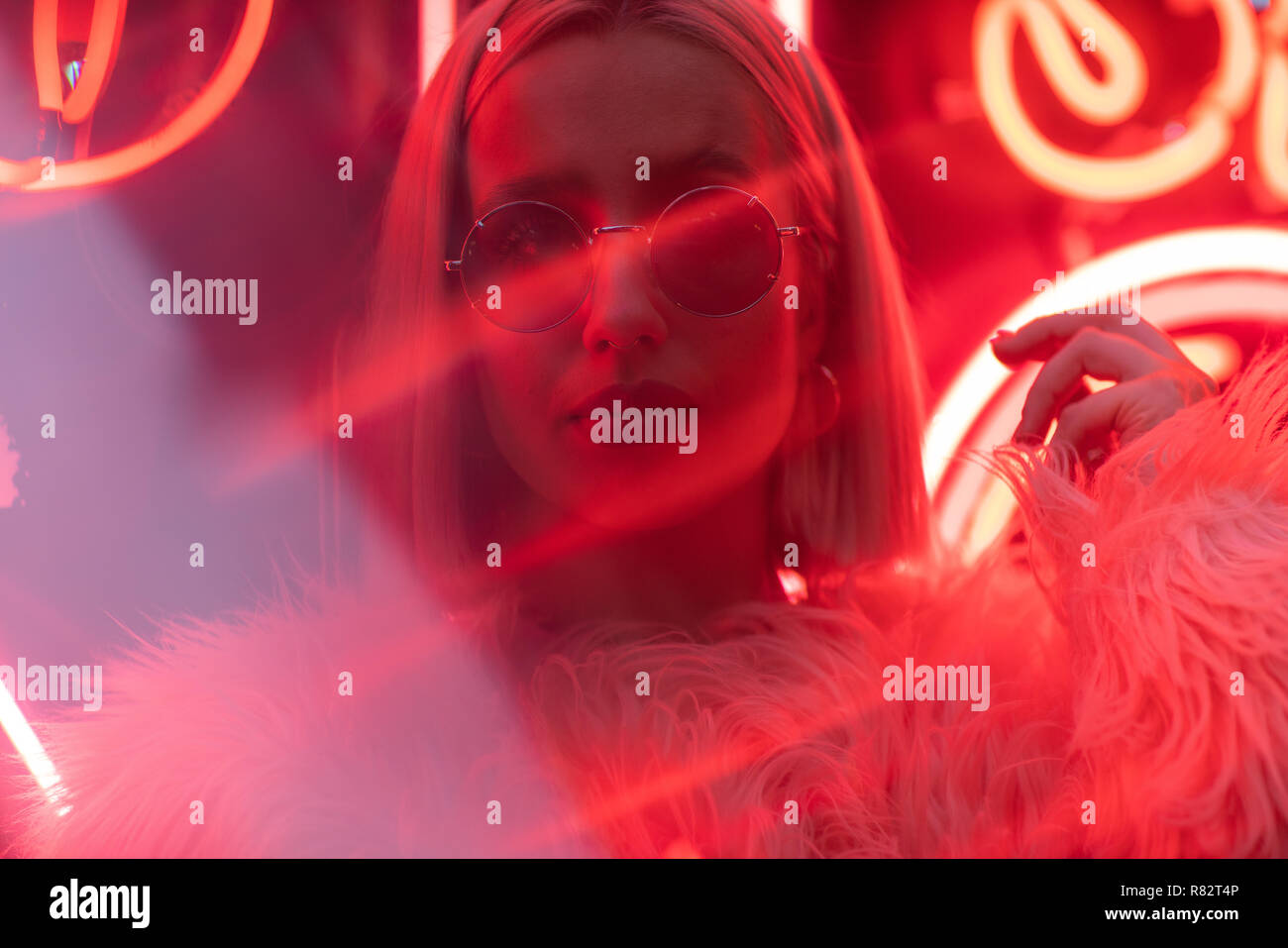 Cinematic portrait of blond girl with furry pink coat on neon sign at ...