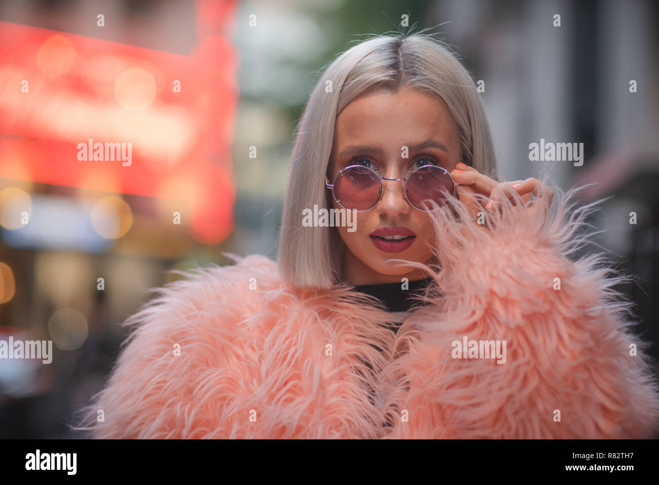 Cinematic portrait of blond girl with furry pink coat on neon sign at ...