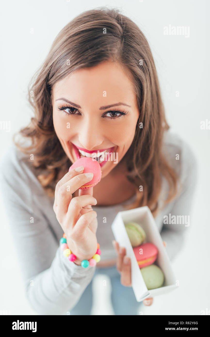 Beautiful young smiling woman biting macaroon. Looking at camera Stock ...