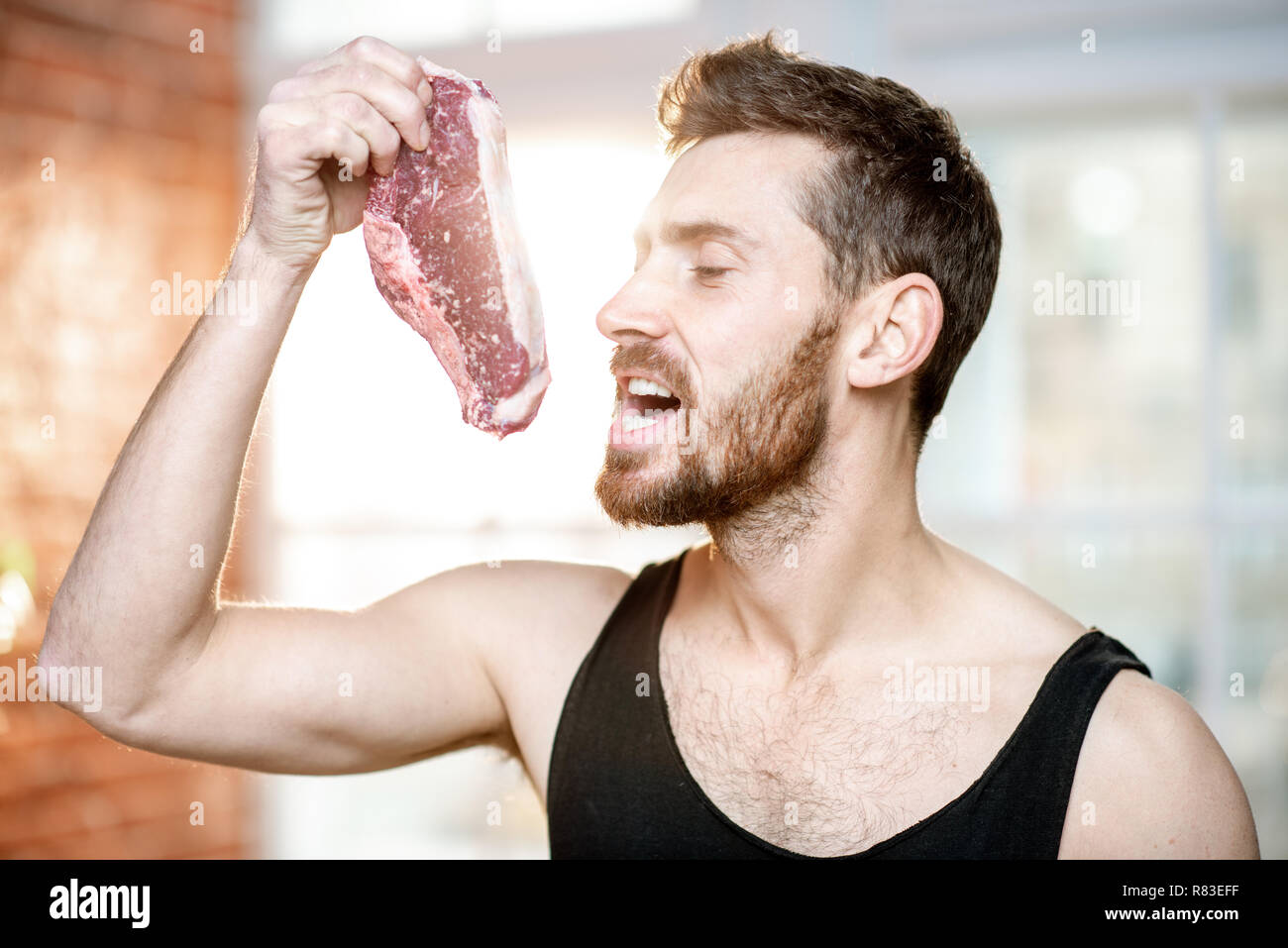 Portrait of a handsome sports man in black t-shirt biting raw meat ...