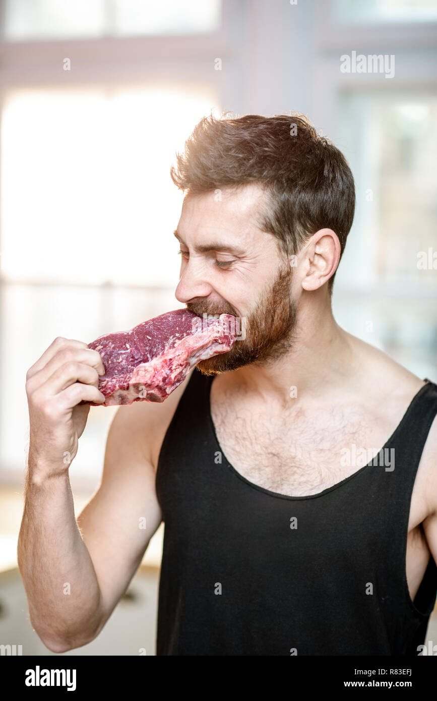 Portrait of a handsome sports man in black t-shirt biting raw meat ...